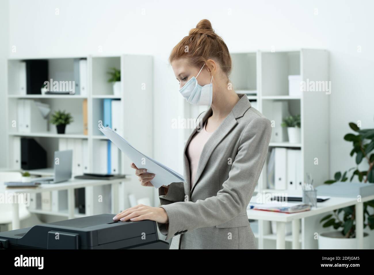 Young businesswoman in elegant grey suit and protective mask looking ...