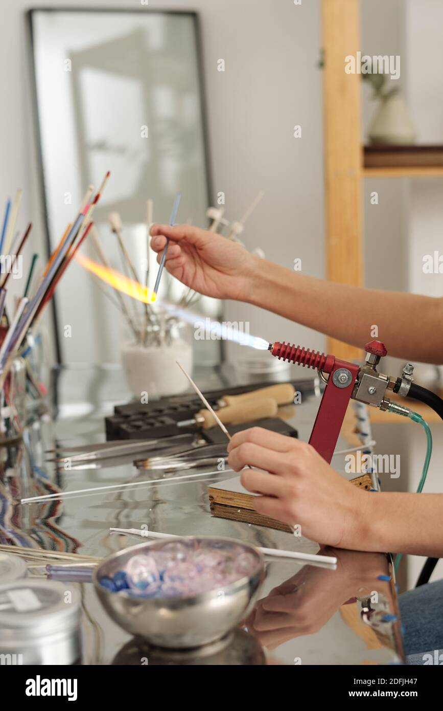 Hands of young professional lampworker sitting by workplace and burning ...