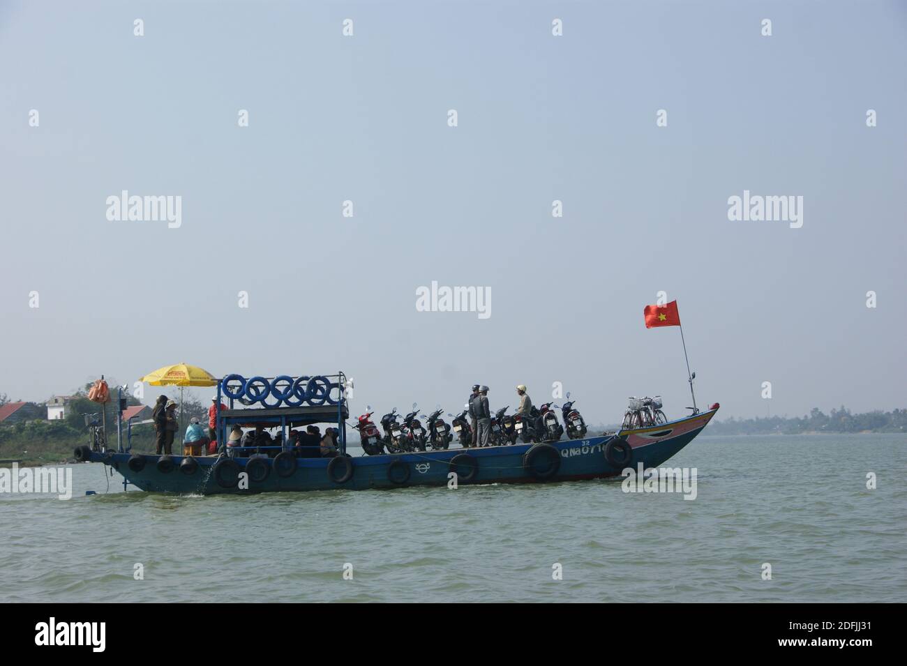 Vietnamese flag flies from the prow of a ferry crossing a wide river ...