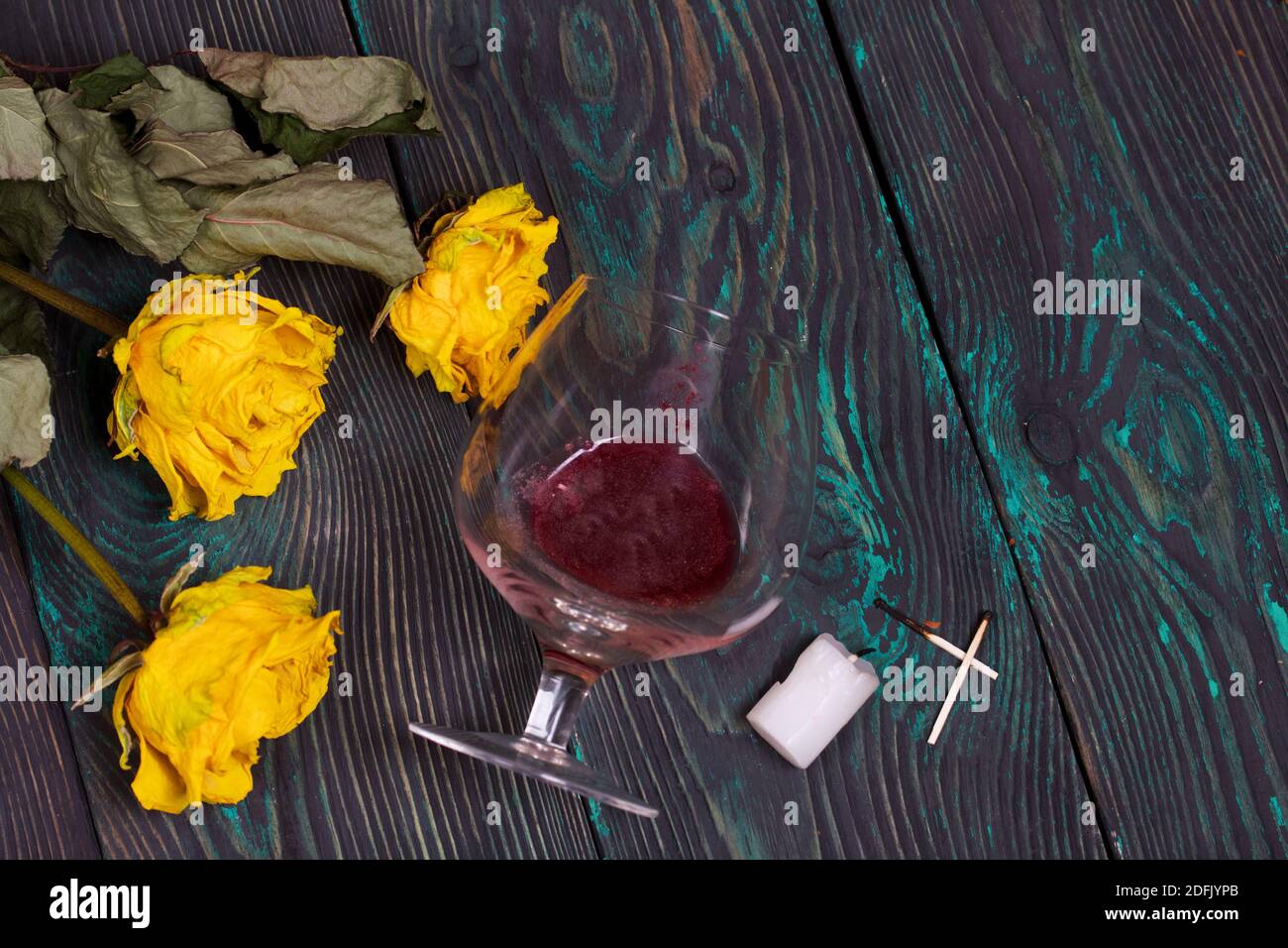 A bouquet of dried yellow roses and candle stubs. An overturned glass ...