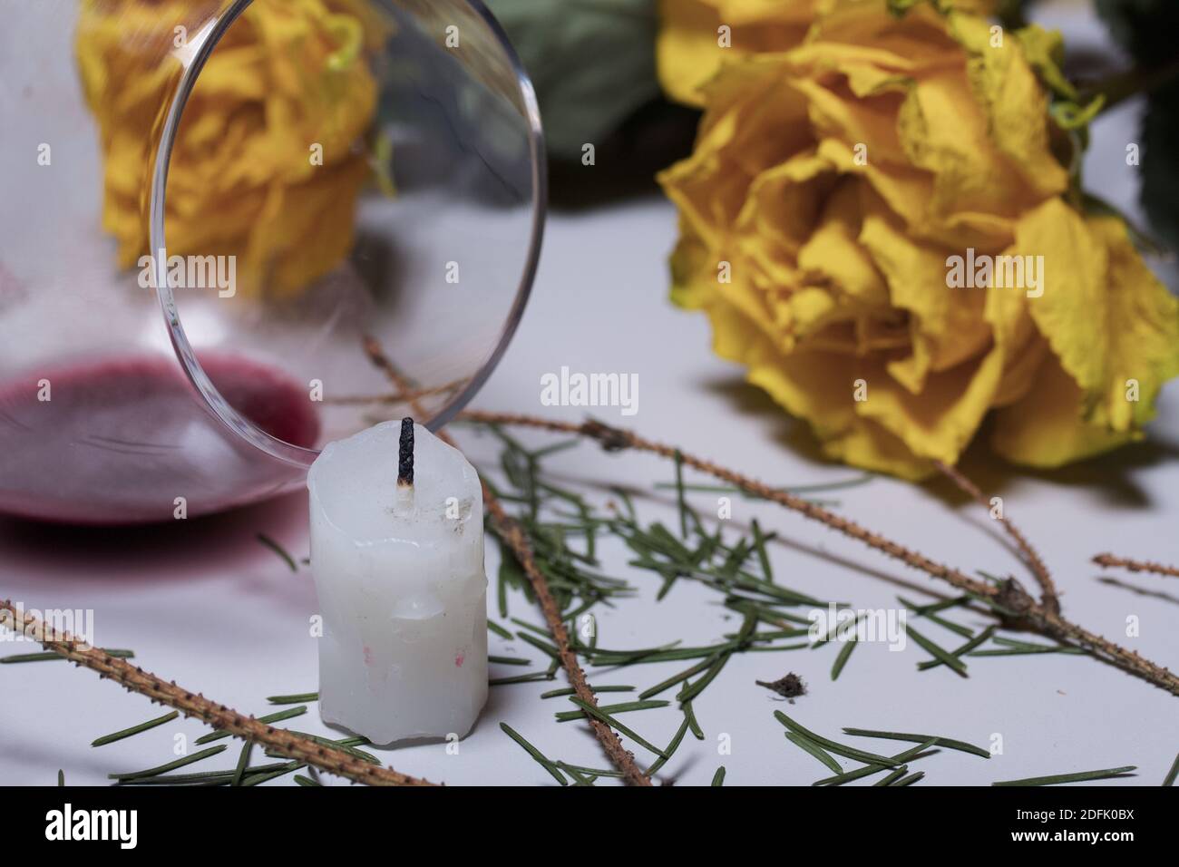 A bouquet of dried yellow roses and candle stubs. An overturned glass ...