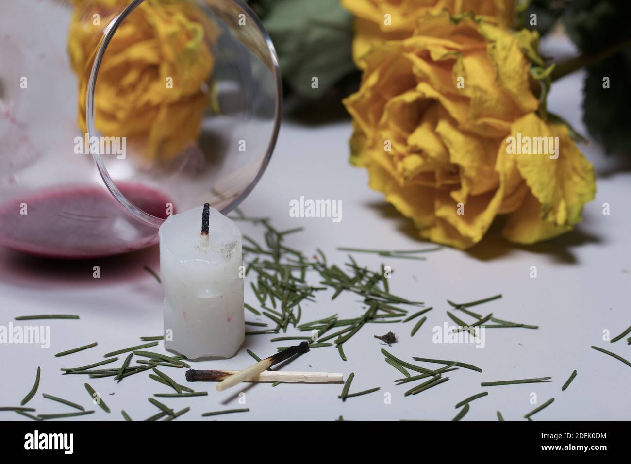 A bouquet of dried yellow roses and candle stubs. An overturned glass ...