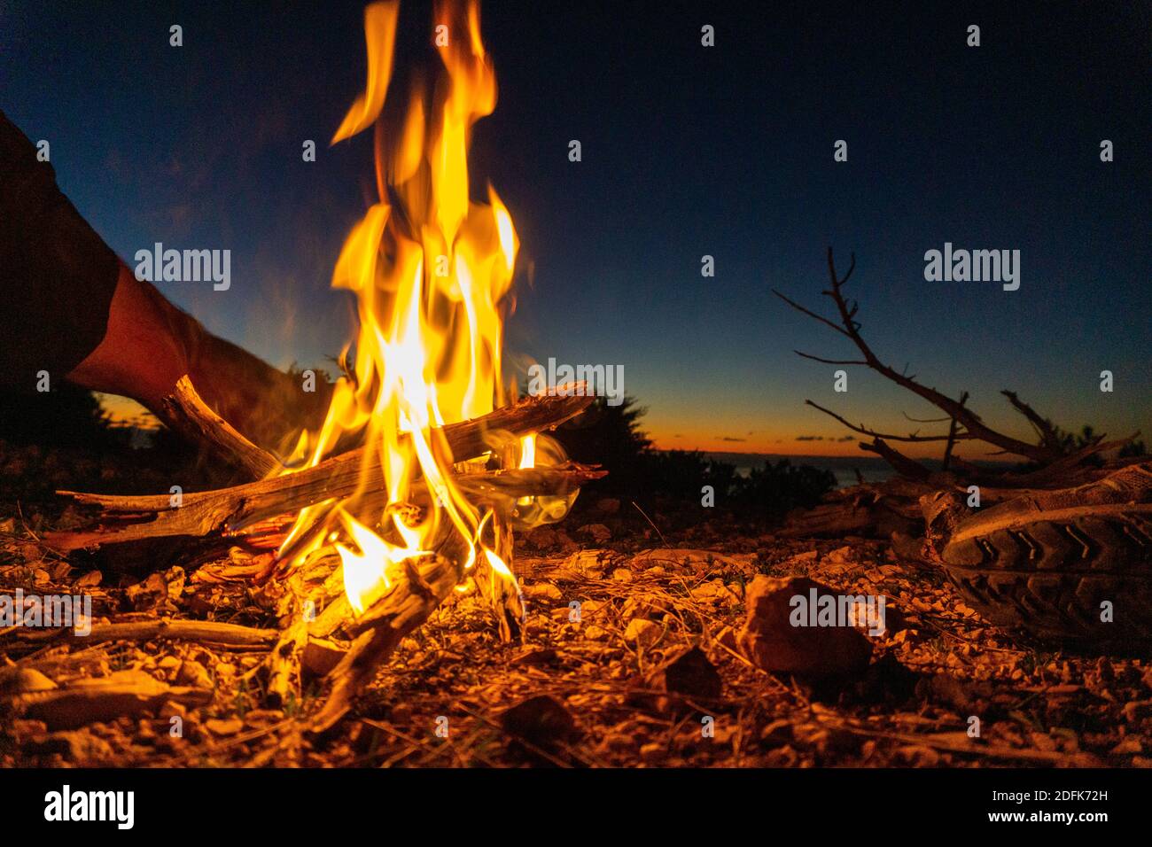 Small camp fire burning at sunset near the sea with legs and feet of ...