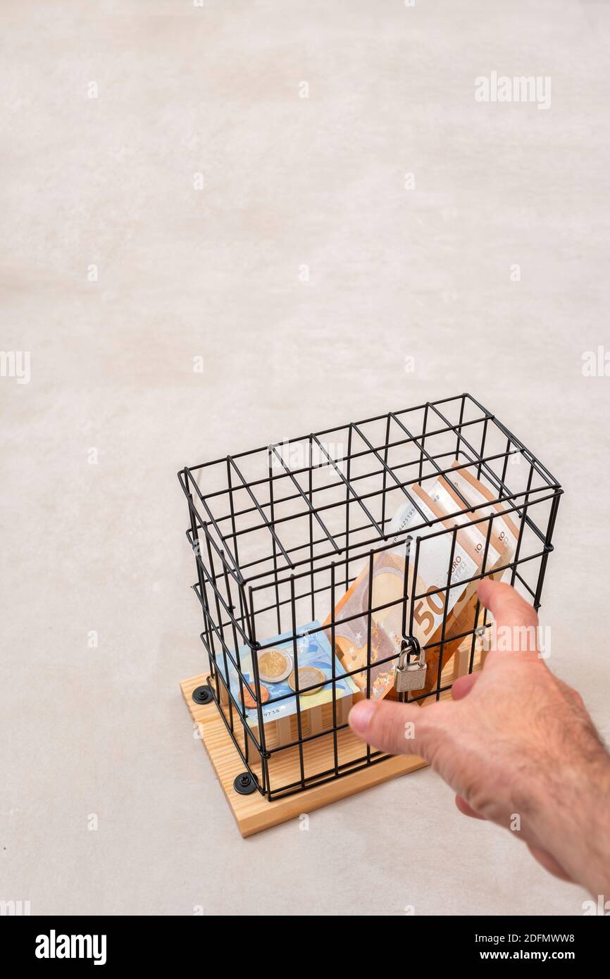hand trying to pick up some banknotes that are inside a cage, white ...