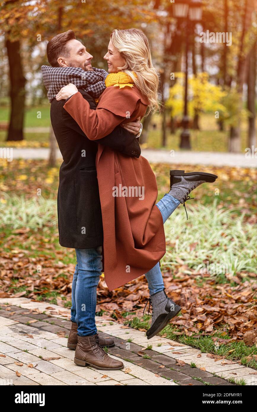 Husband lifting a wife hugged laughing in the autumn park with a cute ...