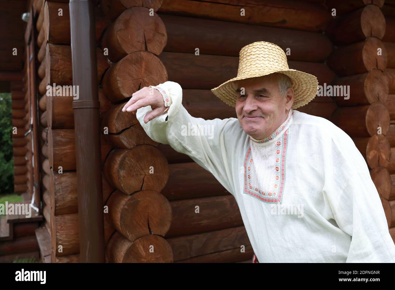 Senior man in traditional Belarusian clothes on background of log cabin ...