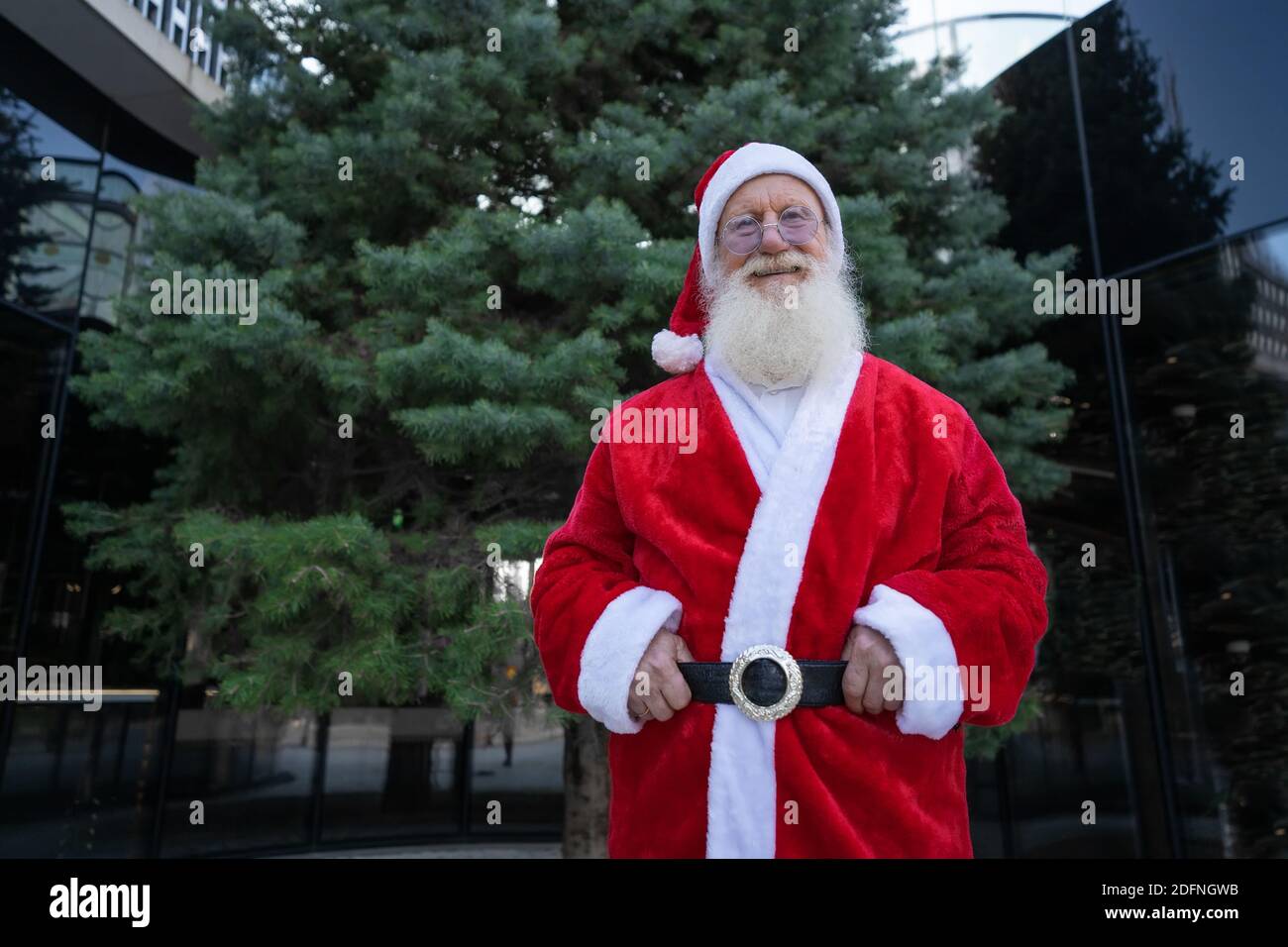 Positive and happy Santa Claus looks on camera. Man stands in front of ...