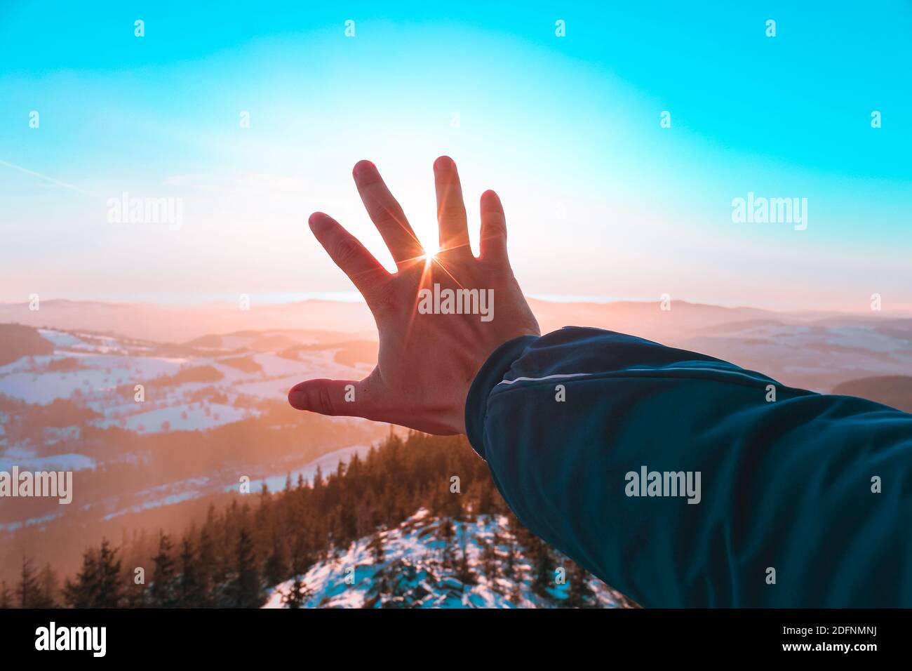 Male right hand covering the sun in Czechia mountines covered with snow ...