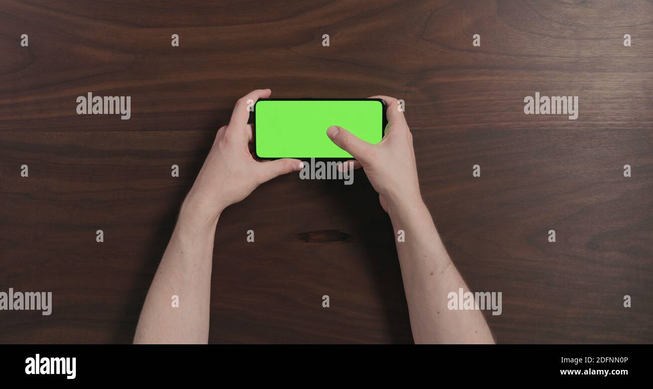 Top view man hand use smartphone with green screen over black walnut ...