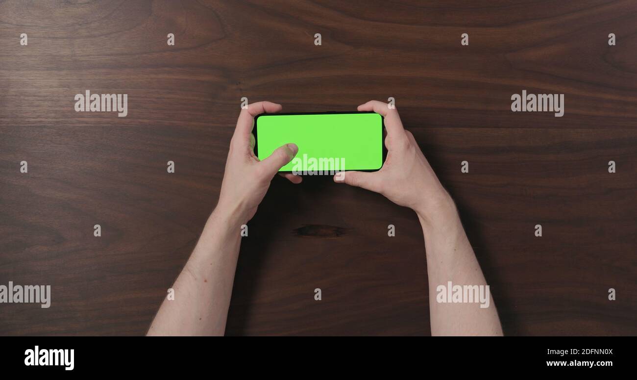 Top view man hand use smartphone with green screen over black walnut ...