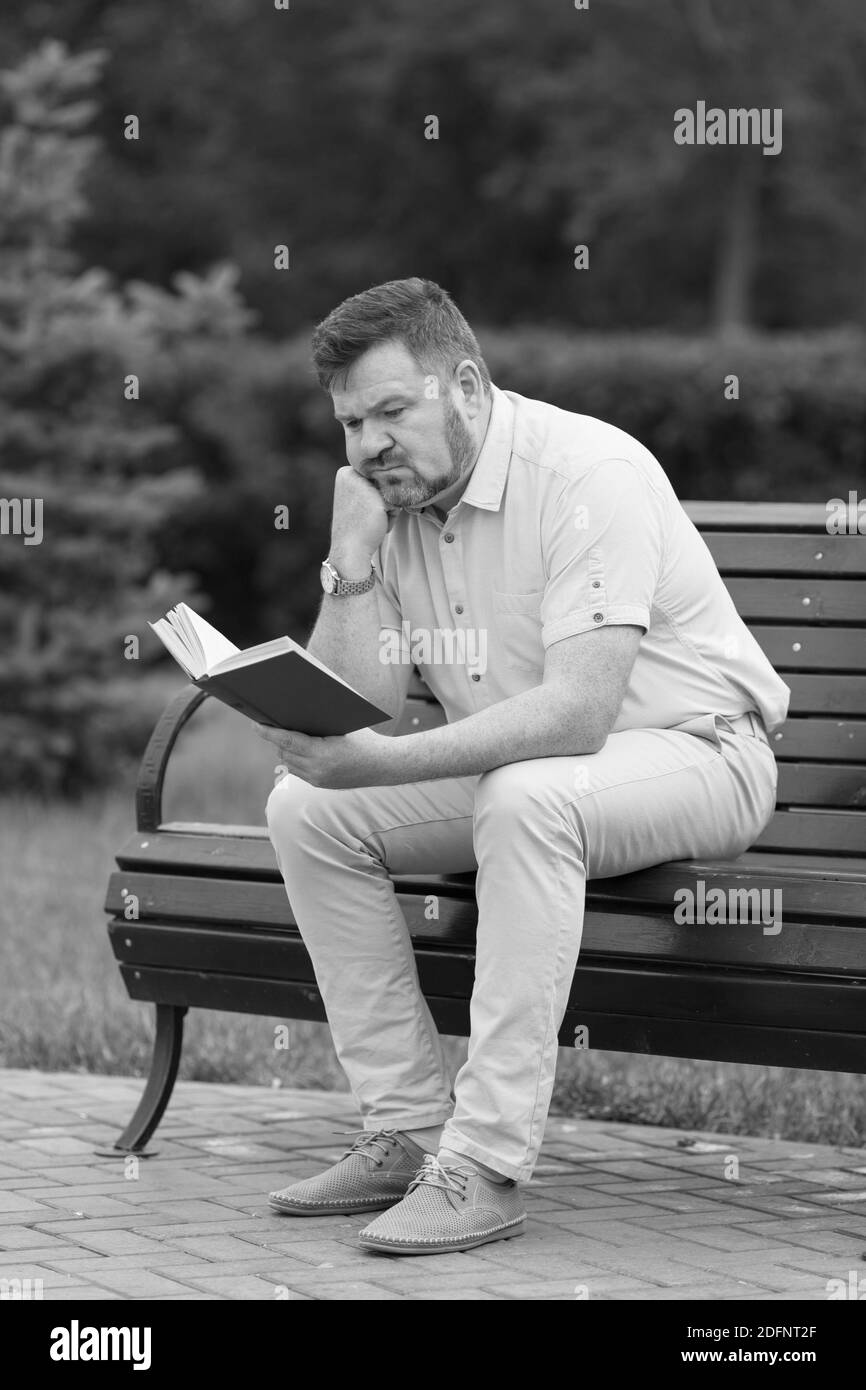 Lonely man reading a book on the bench in his spare time. Black and ...