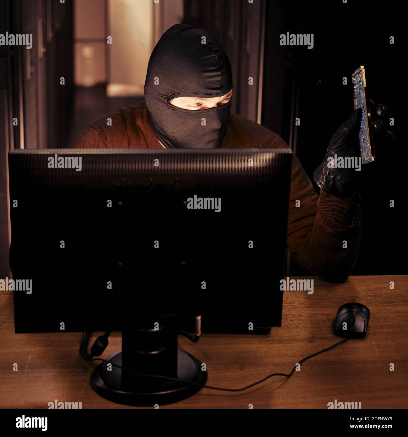 Hacker in black balaclava with a printed circuit board from the device ...