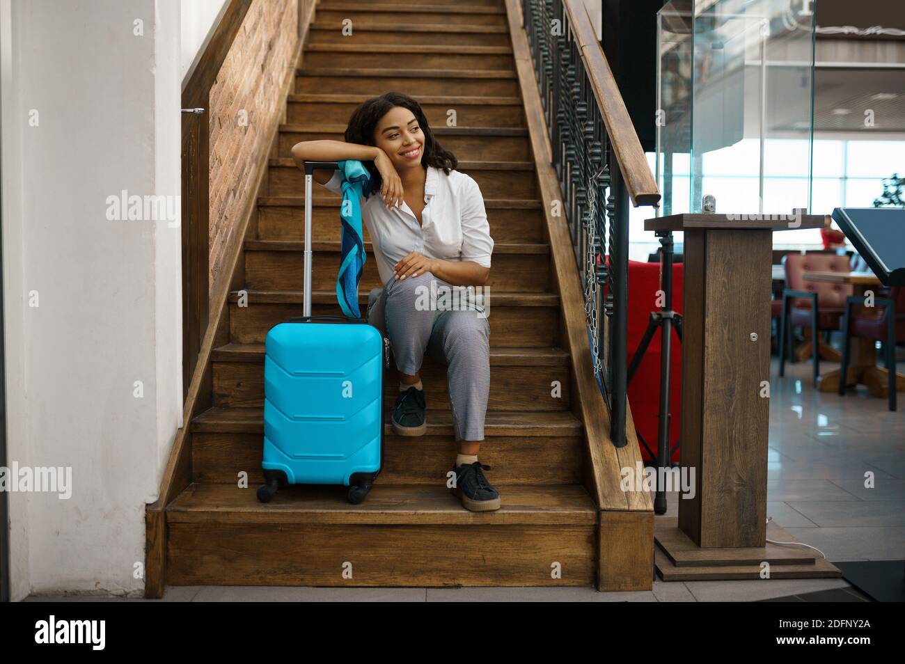 Woman with suitcase sitting on stairs in airport Stock Photo - Alamy