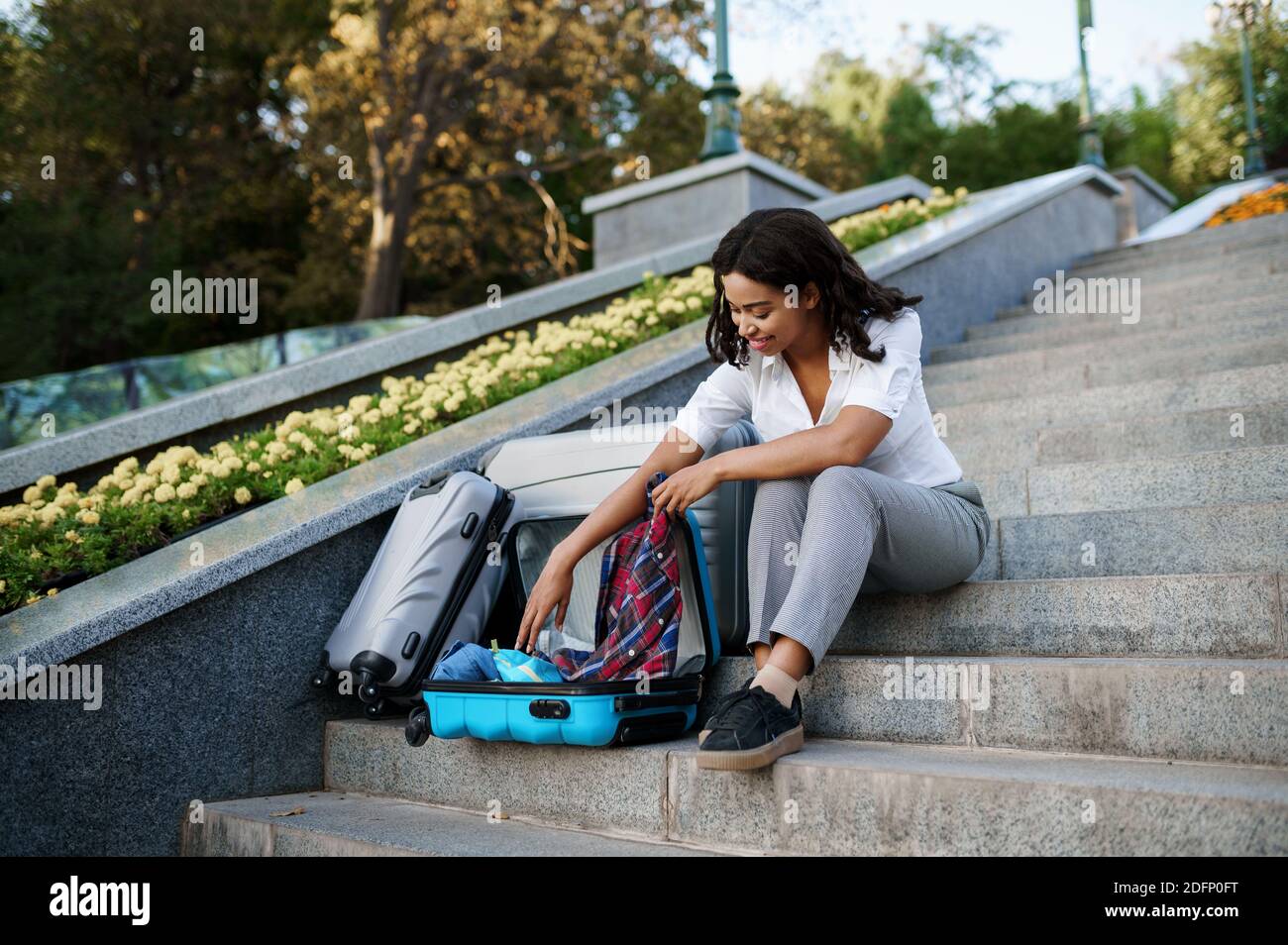 Woman opens suitcase on the stairs in summer park Stock Photo - Alamy