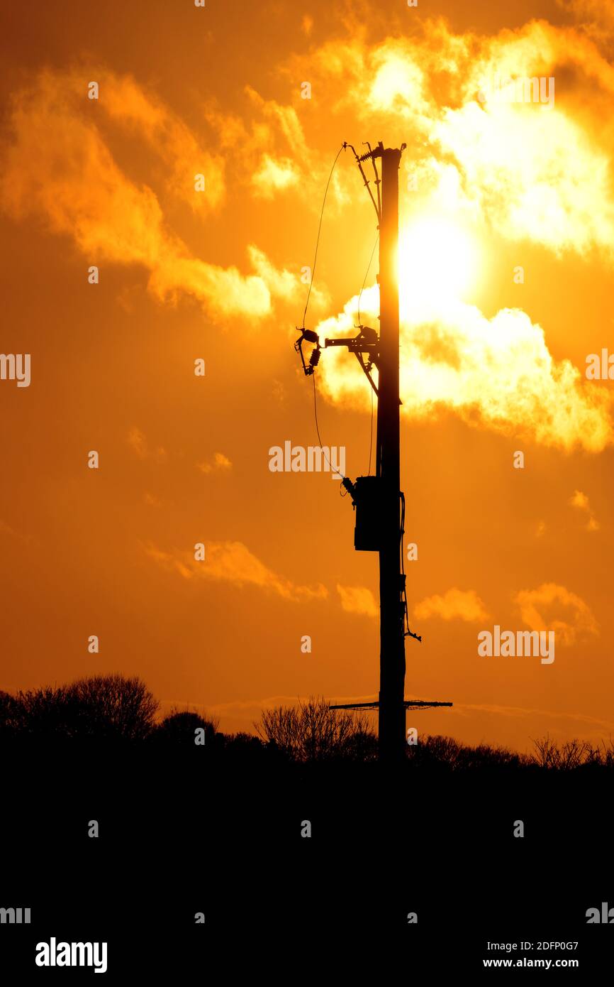 Power comms cable and transmission lines and pole against orange sunset ...
