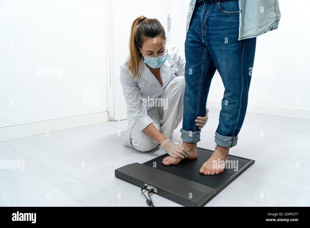 Young podiatrist in her clinic examining a patient's feet on a pressure ...