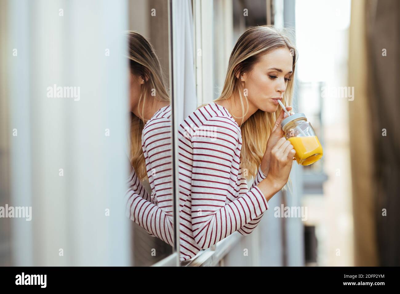 Young woman drinking a glass of natural orange juice, leaning out the ...