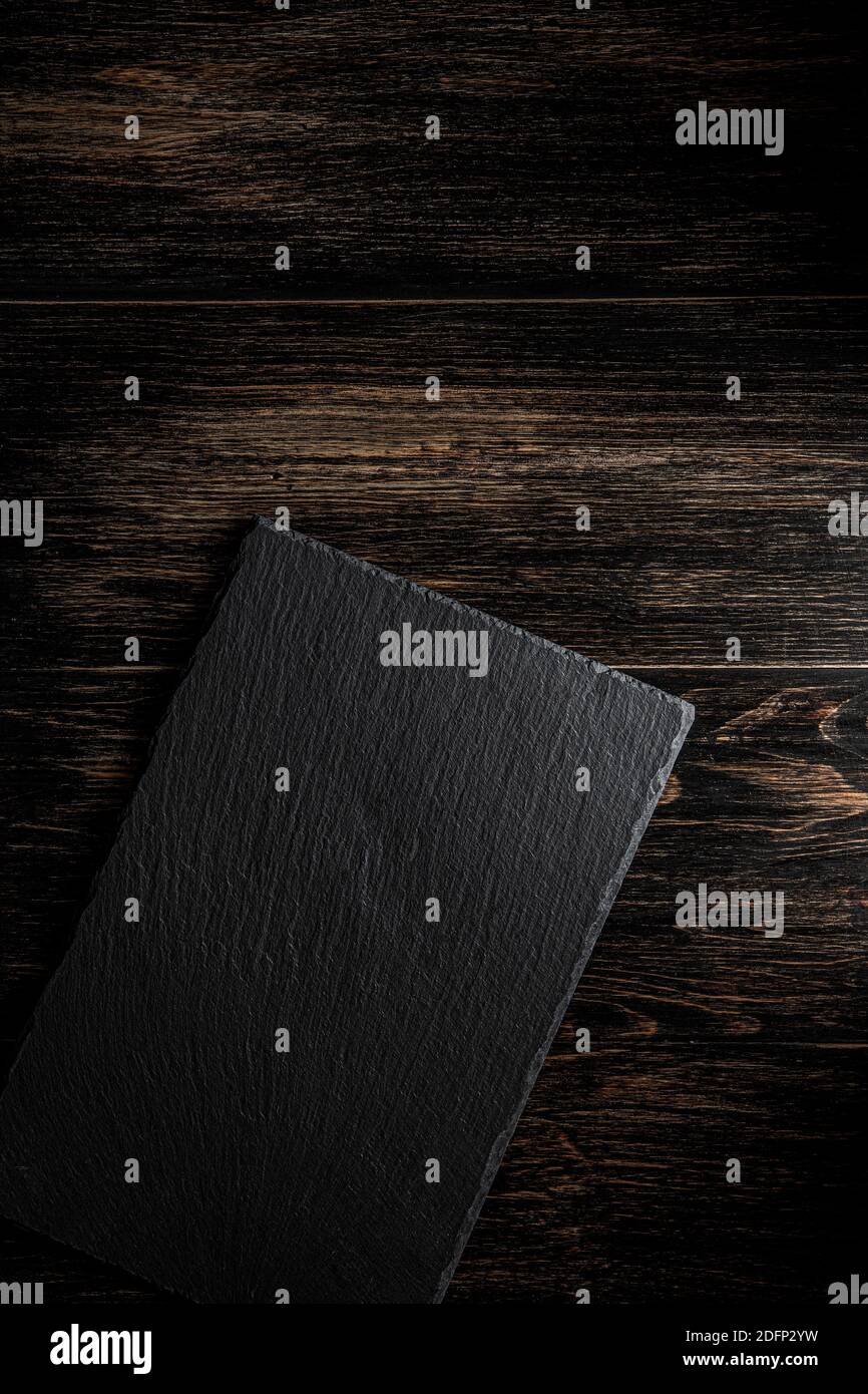 Dark gray slate plate on vintage brown wooden background. Table setting ...