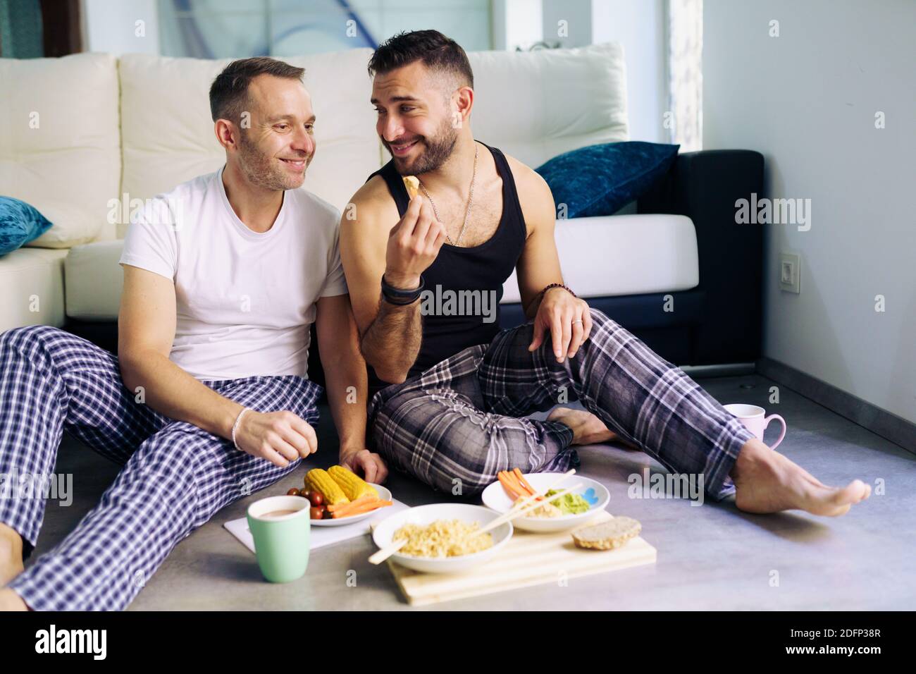 Gay couple eating together sitting on their living room floor Stock ...