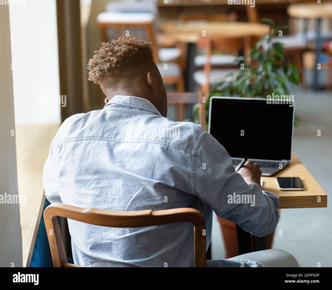 Back view of young black male student studying online on laptop at city ...