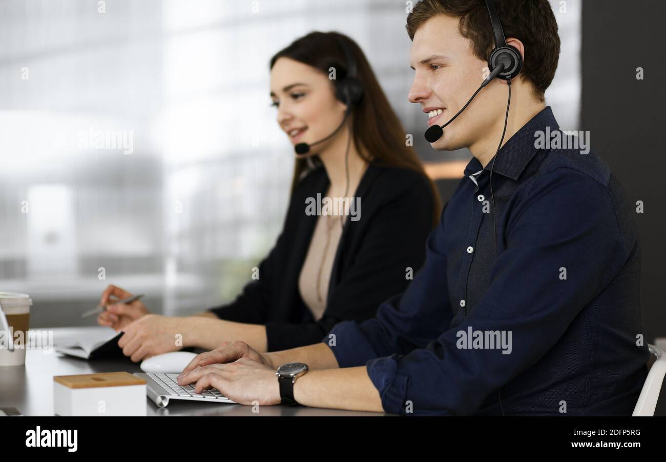 Two young people in headsets are talking to the clients, while sitting ...