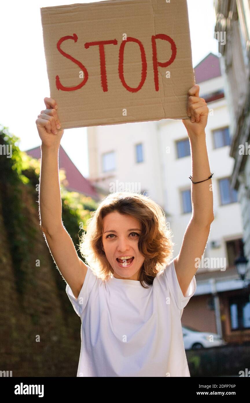 Young protesting woman in white shirt and jeans holds protest sign ...