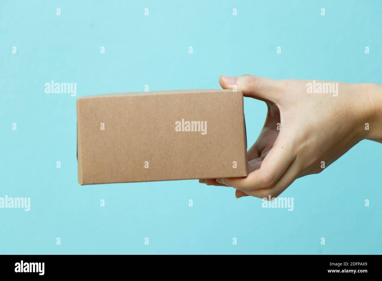 Woman hand hold the brown corrugated box on blue wall background with ...