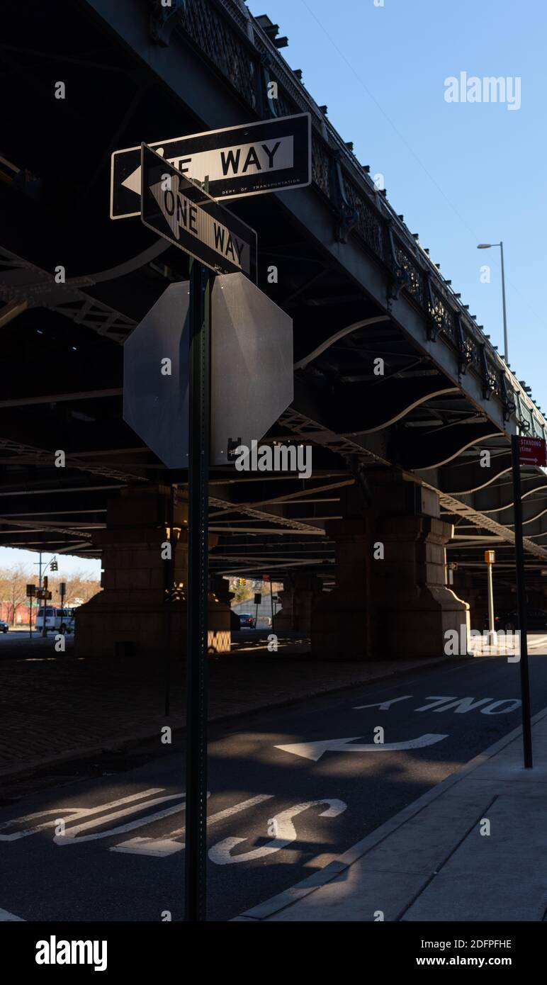 Two 'One Way' signs intersecting under a bridge in dramatic light in ...