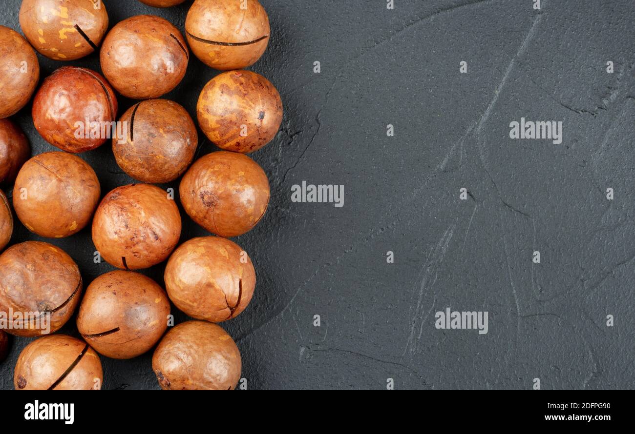 Scattered macadamia nuts in their shells on an empty dark background ...