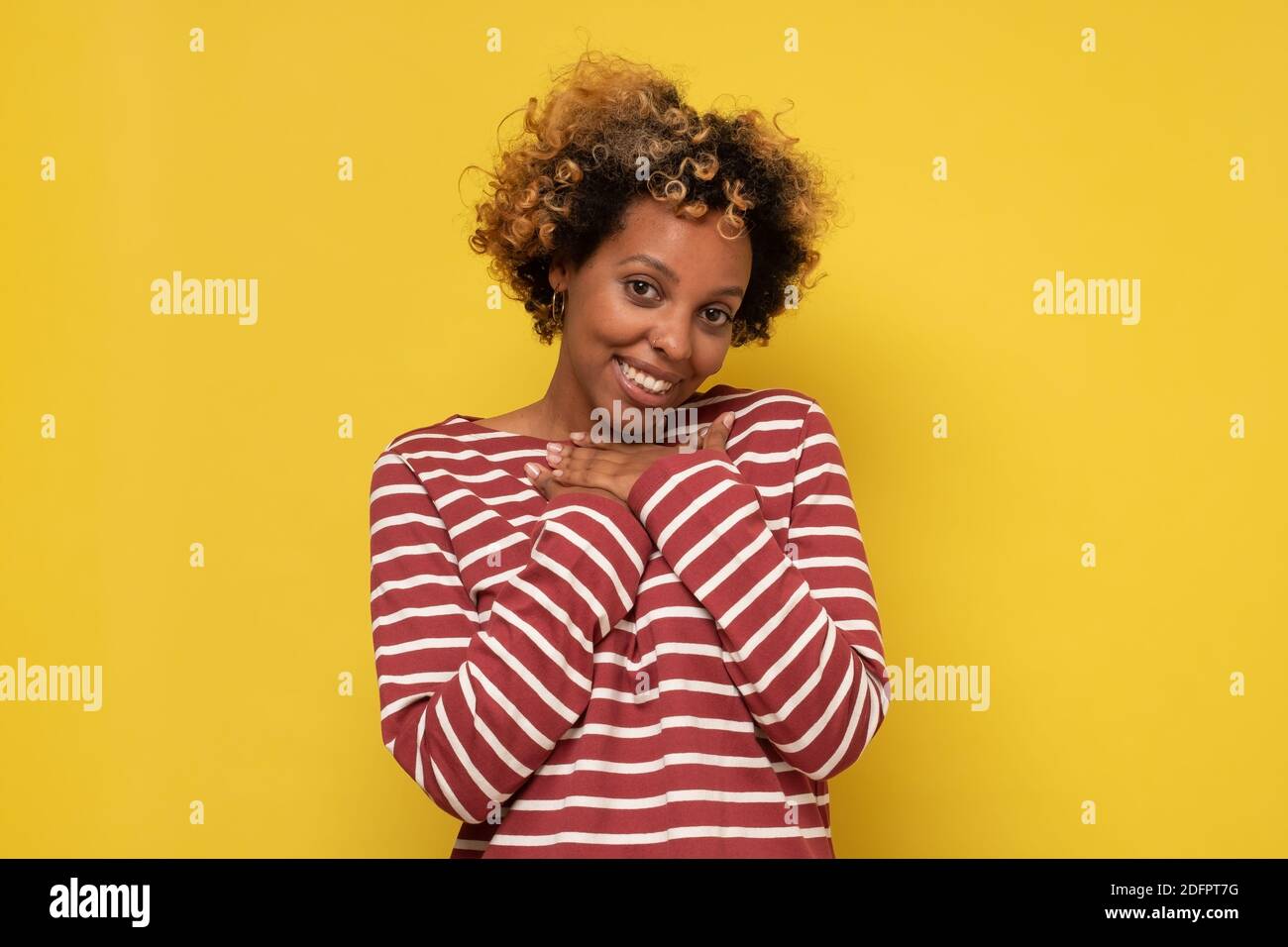 Pleased african woman smiling broadly and keeping hand on her chest ...
