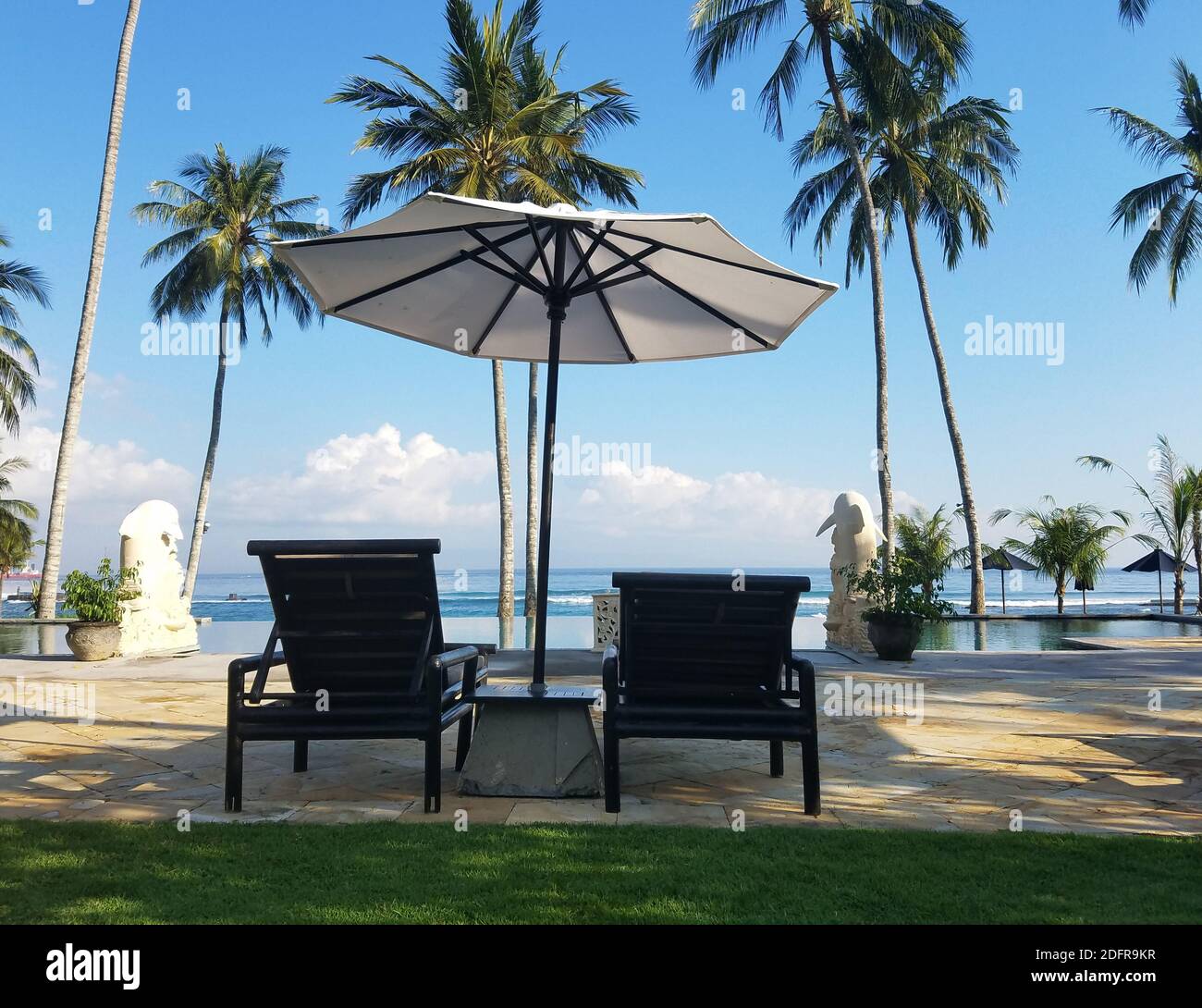 Two pool chaise lounges and an umbrella against an ocean view in Bali ...