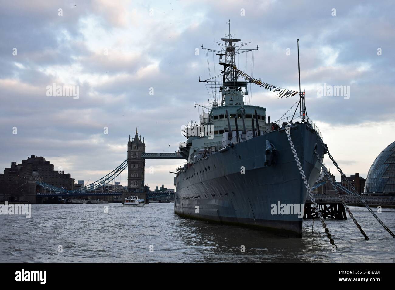 HMS Belfast moored along the River Thames. Behind the warship museum is ...