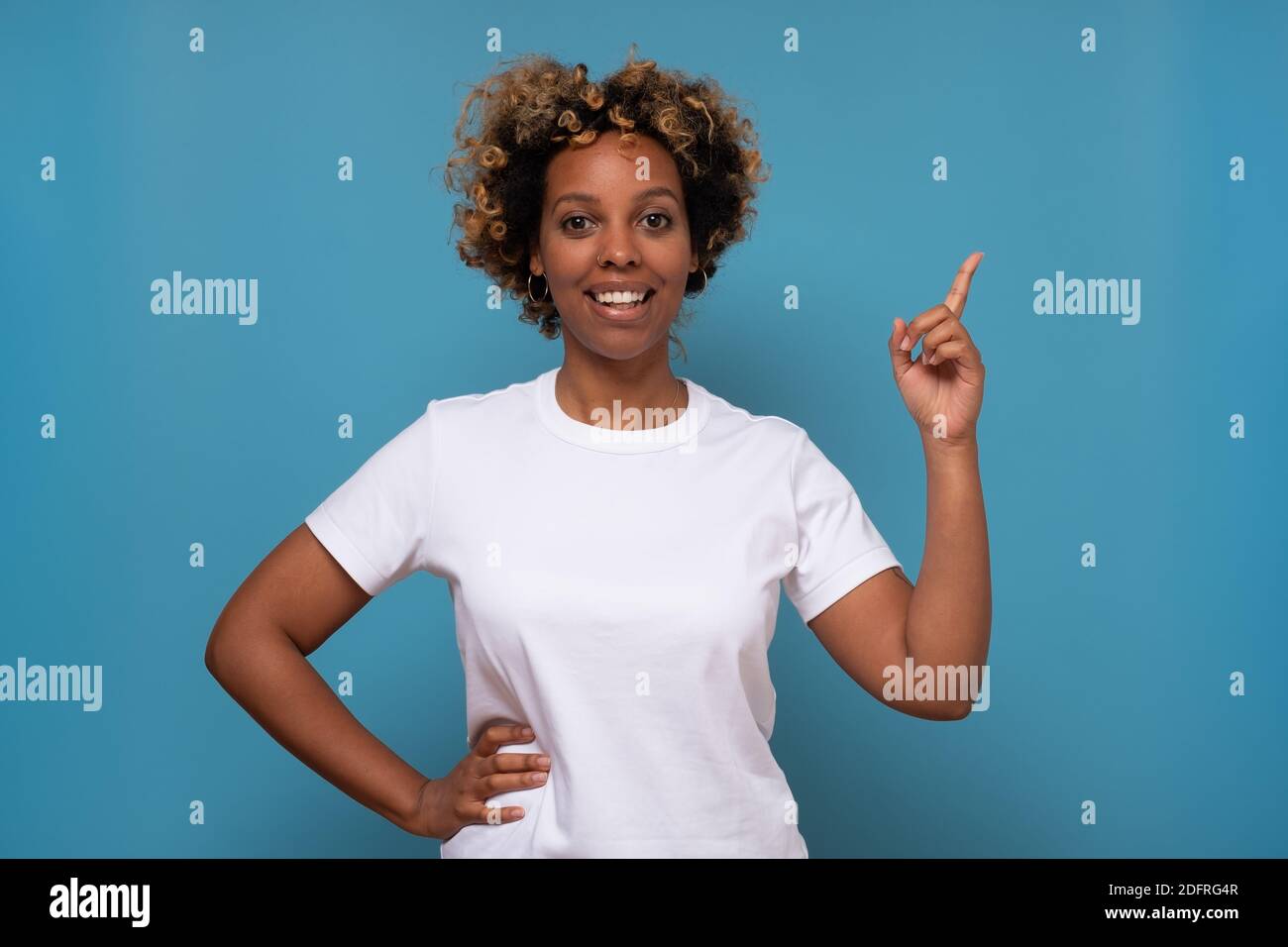 Attractive cheerful african woman with curly hair points aside, shows ...