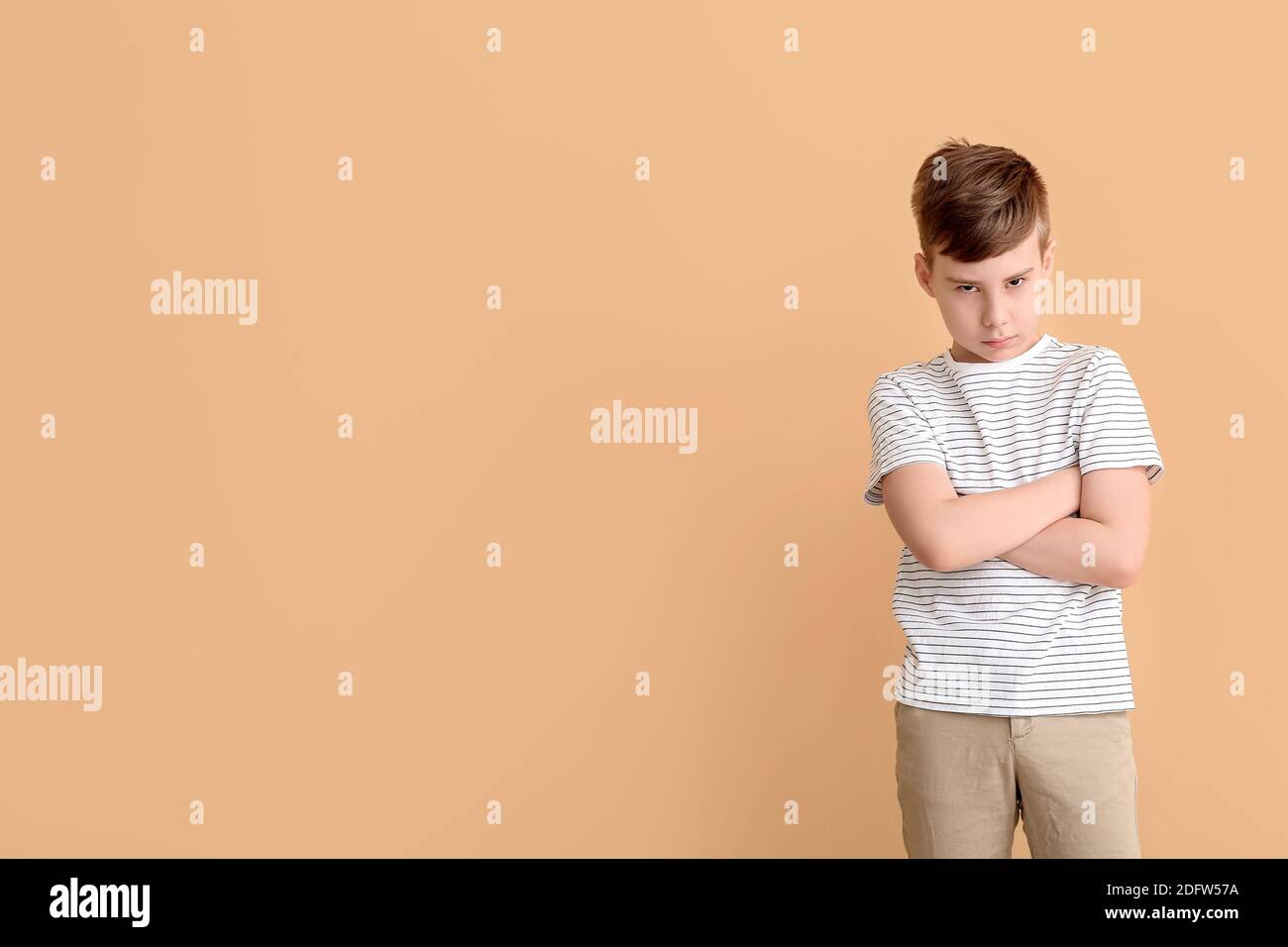 Suspicious cute boy with crossed arms on color background Stock Photo ...