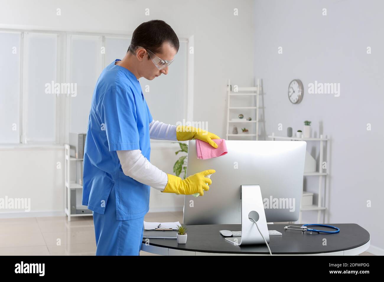 Male janitor cleaning computer in office Stock Photo - Alamy