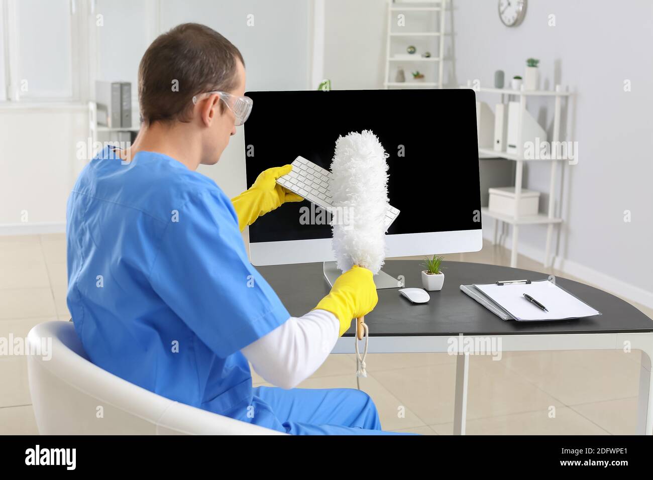 Male janitor cleaning computer in office Stock Photo - Alamy
