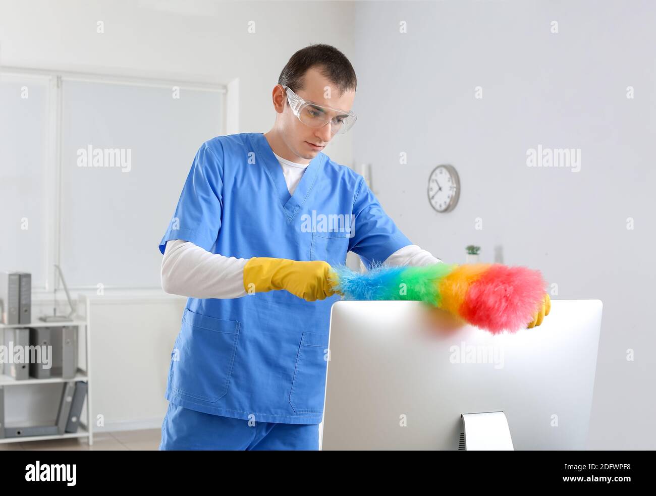 Male janitor cleaning computer in office Stock Photo - Alamy