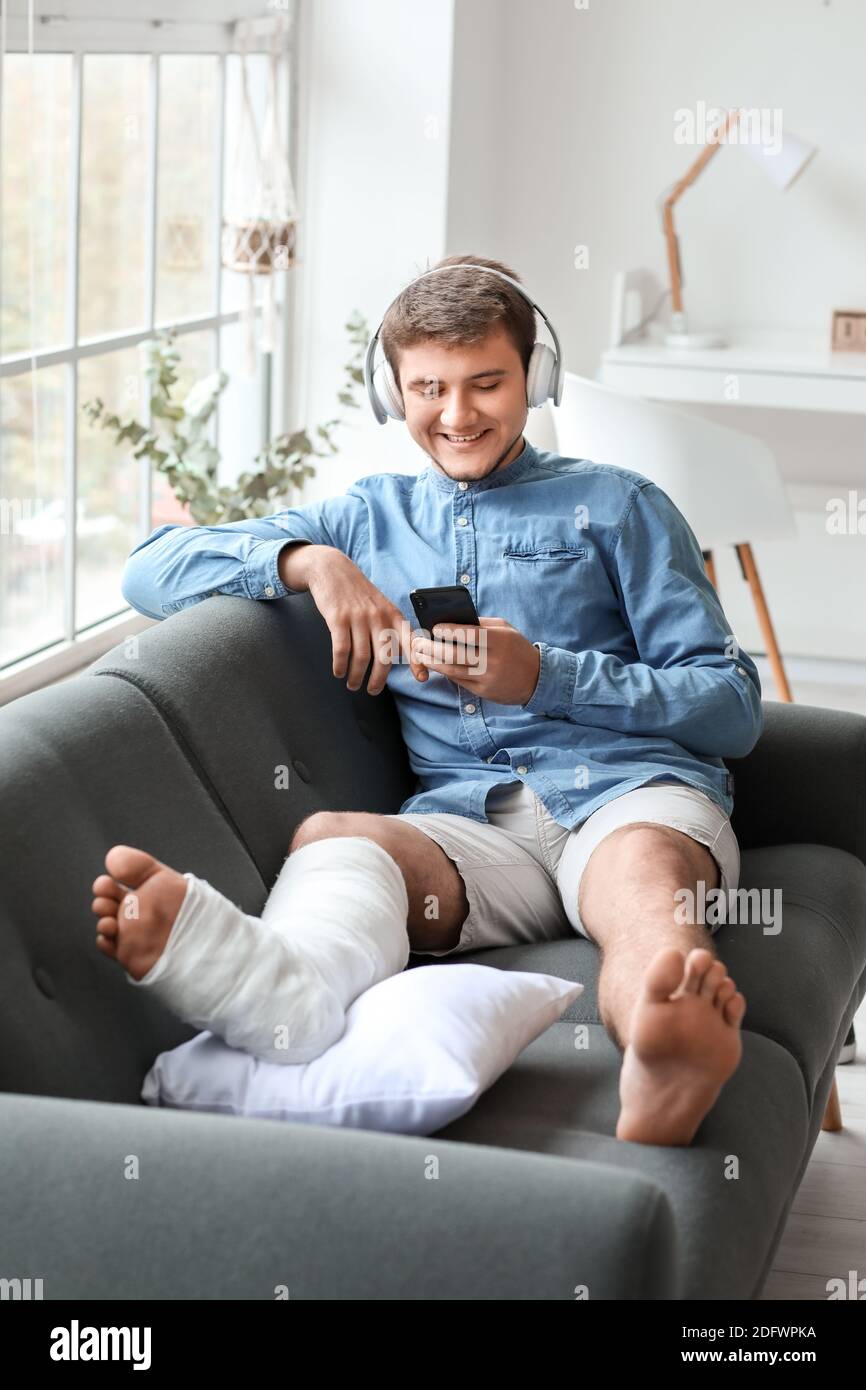 Young man with broken leg listening to music at home Stock Photo - Alamy