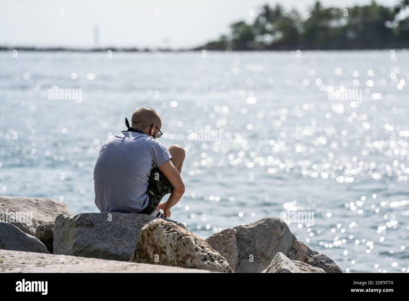 Street photography man sitting on rocks by the bay Miami scene Stock ...