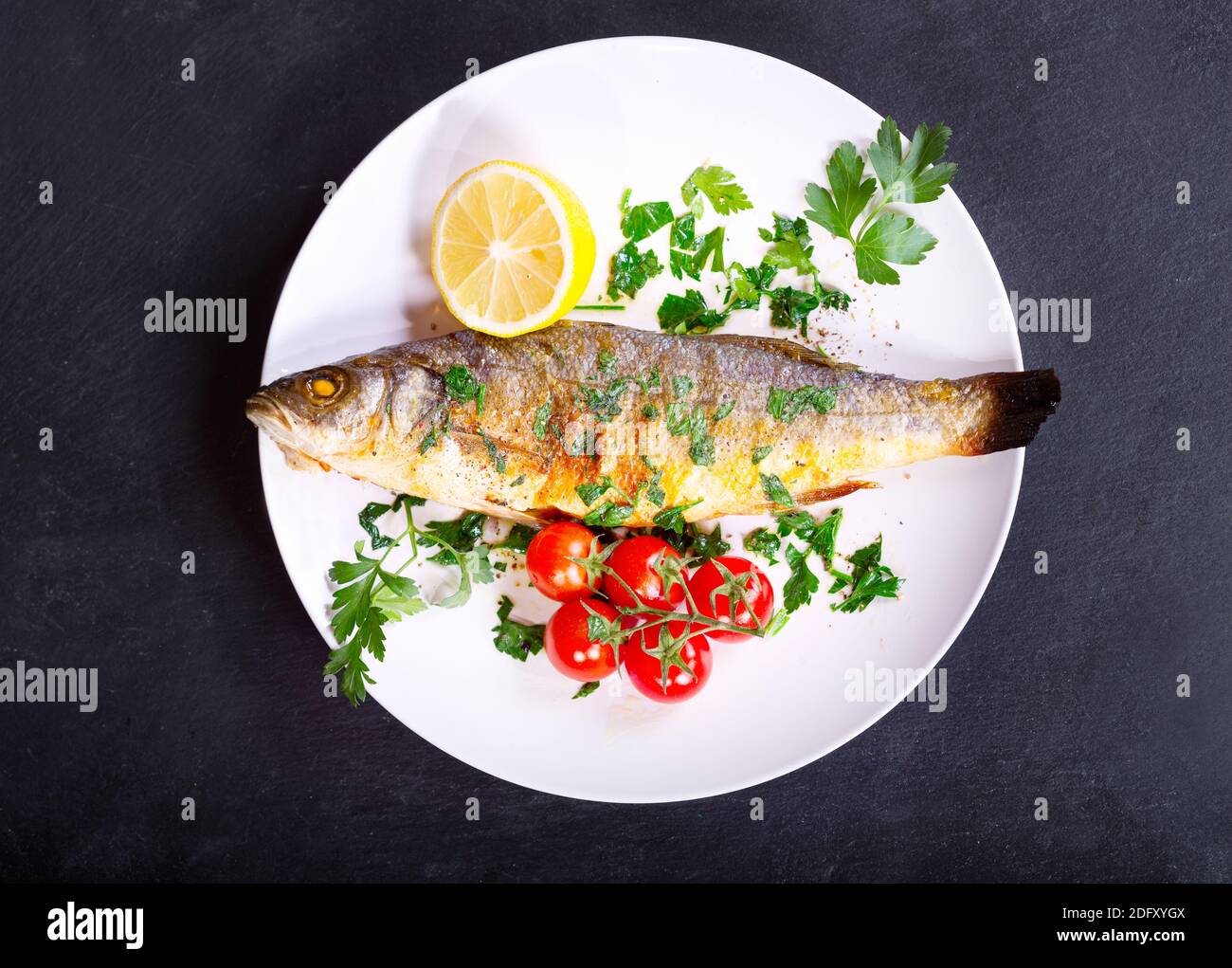 plate of baked sea bass on dark background Stock Photo - Alamy
