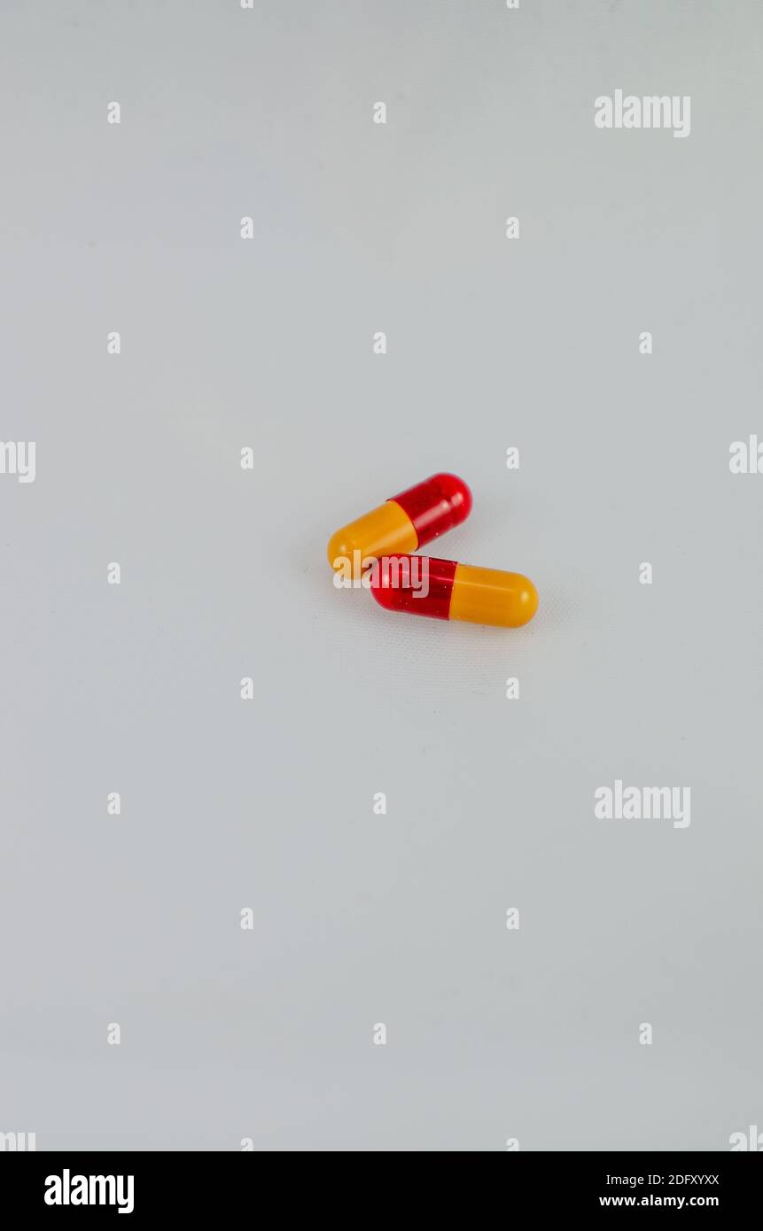 close up of two red and yellow pills in front of a white background ...