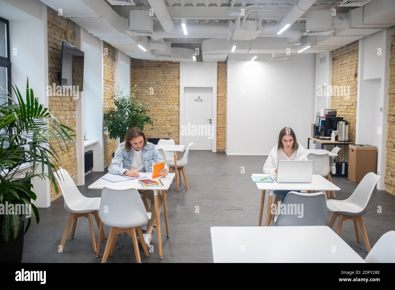 Two colleagues sitting at the tables working in the office Stock Photo ...