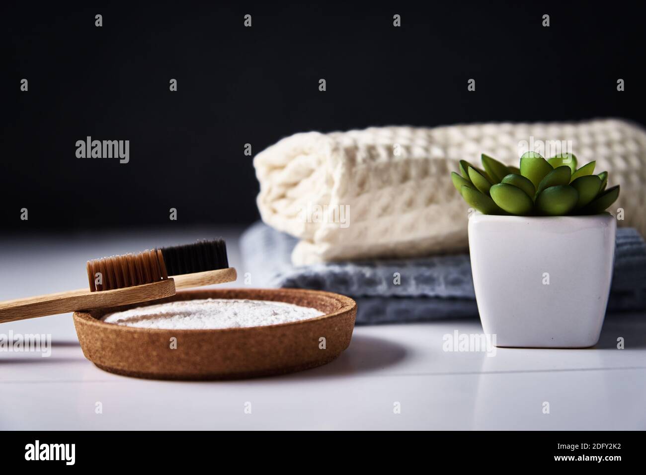 Bamboo toothbrushes, baking soda and bathroom towels on a dark ...