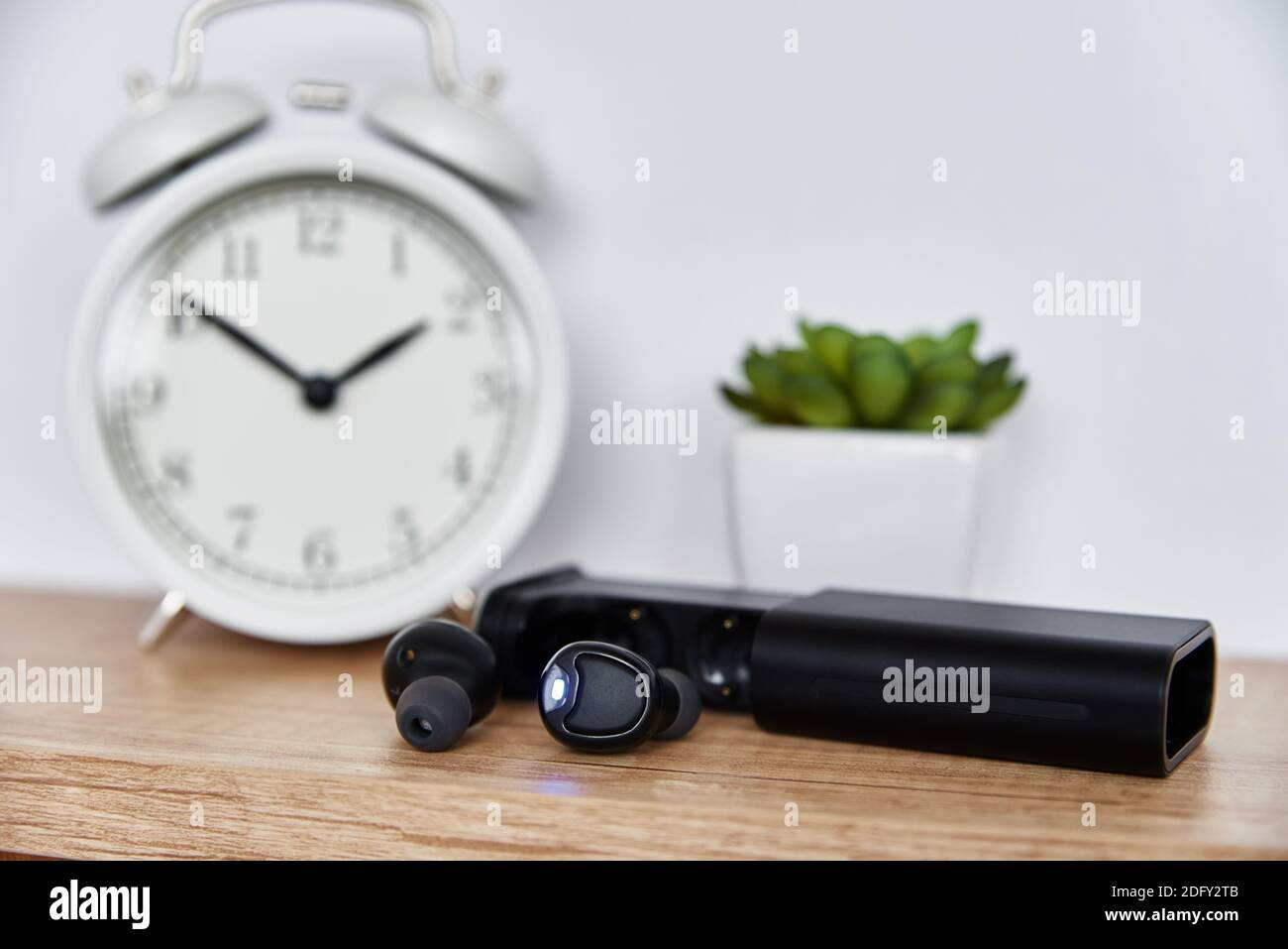 Wireless earphones on the shelf with alarm clock and house plant ...