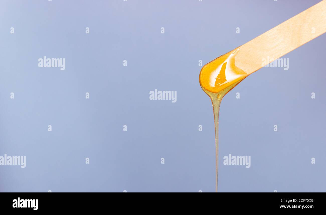 Sugar depilatory paste drips from a wooden spatula. The removal of body ...