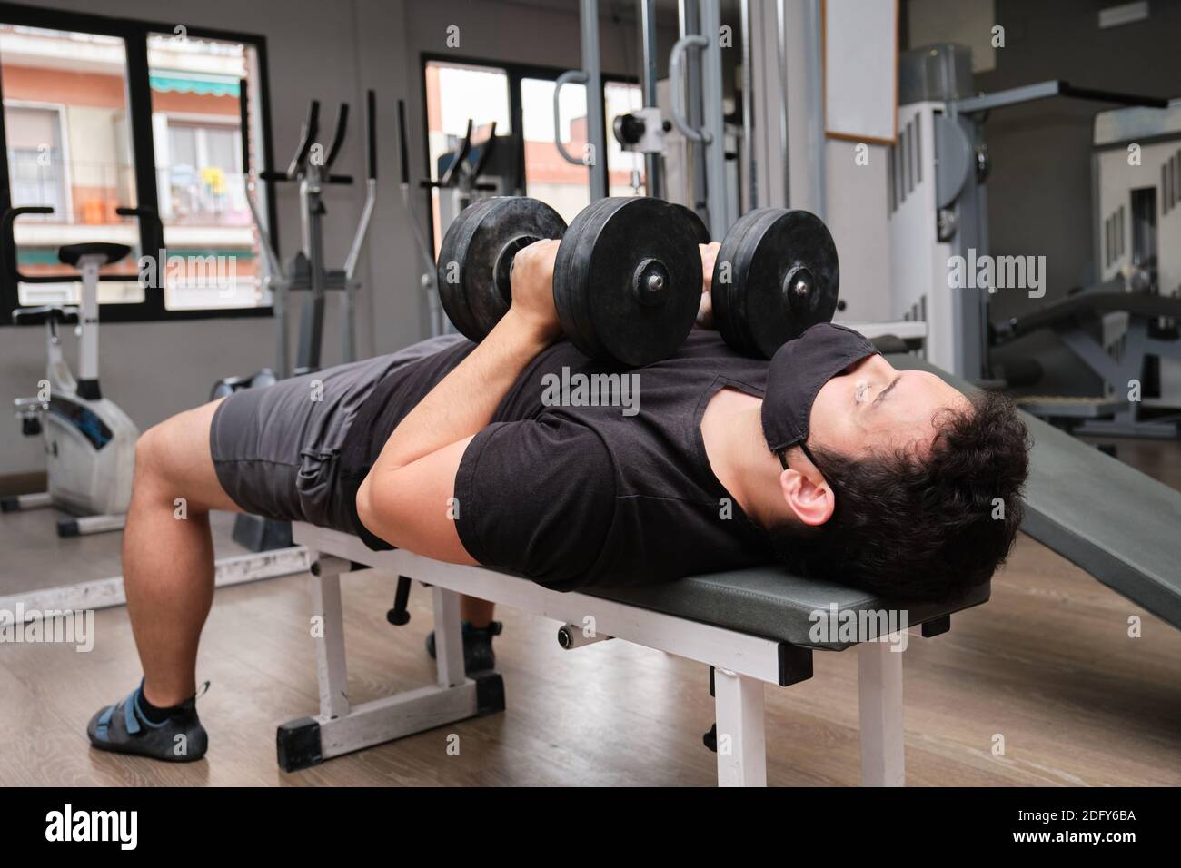 Strong man wearing face mask lifting dumbbells at gym. Weight lifting ...