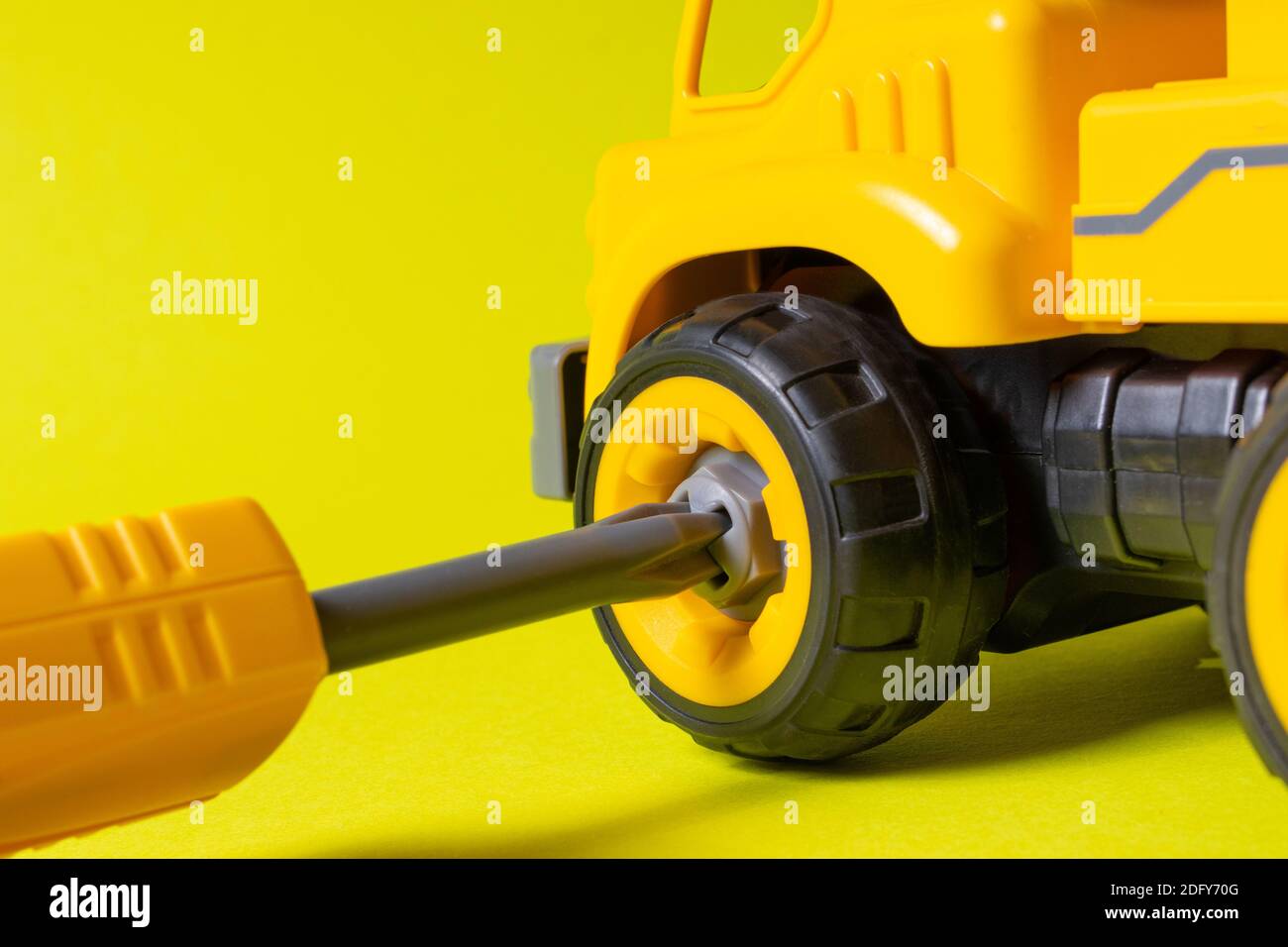 The screwdriver unscrews the wheel of the toy car on a yellow ...