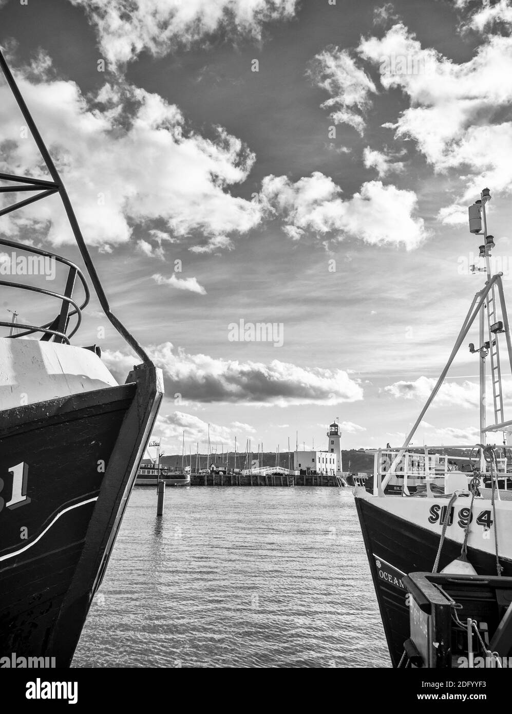 A lighthouse and pier are glimpsed between the bows of two trawlers ...