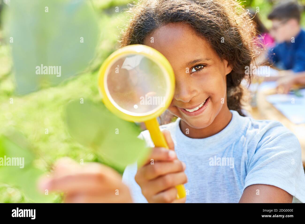 Happy girl in summer school at summer camp looks through magnifying ...