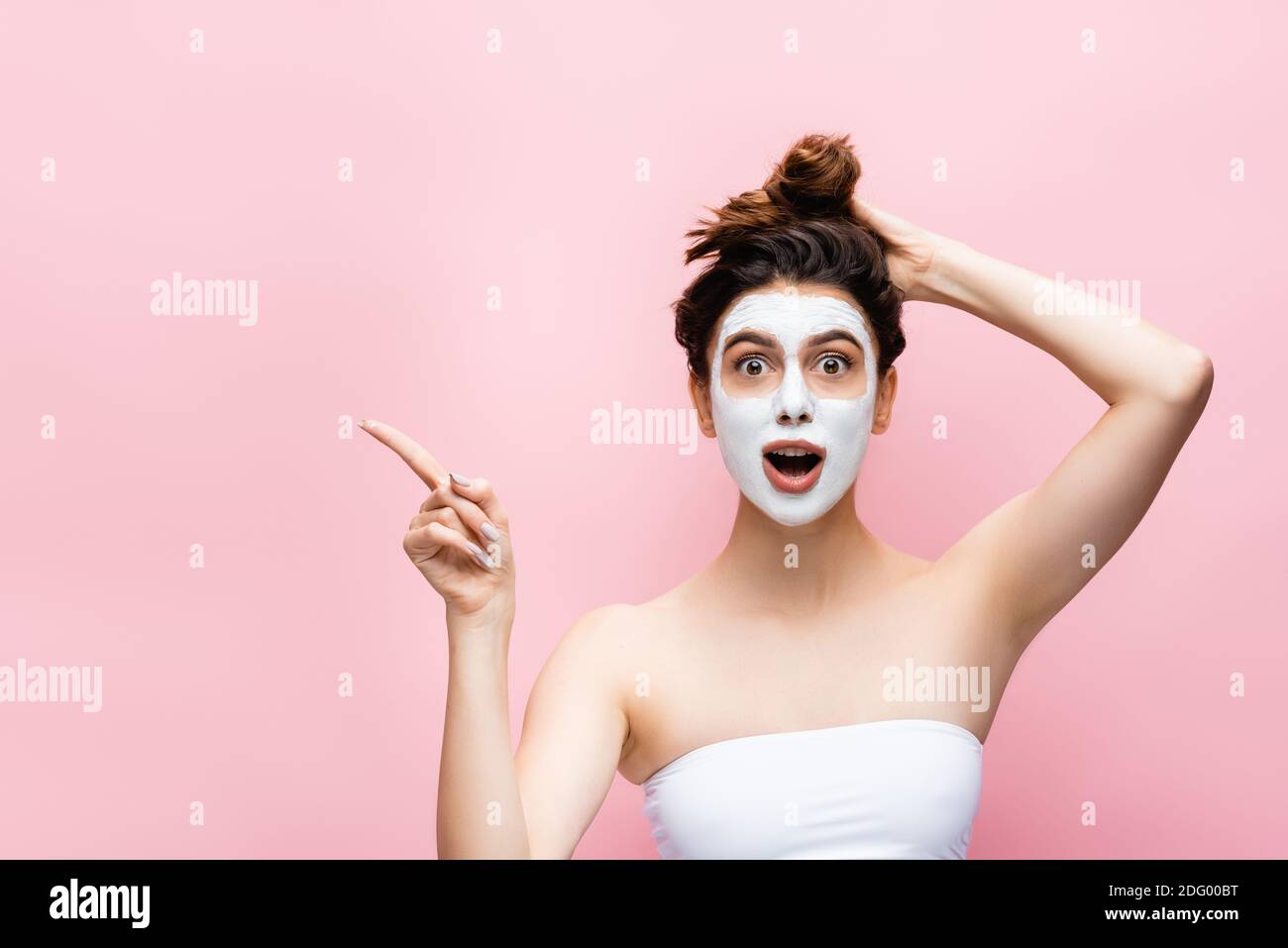 shocked beautiful woman with clay mask on face pointing aside isolated ...